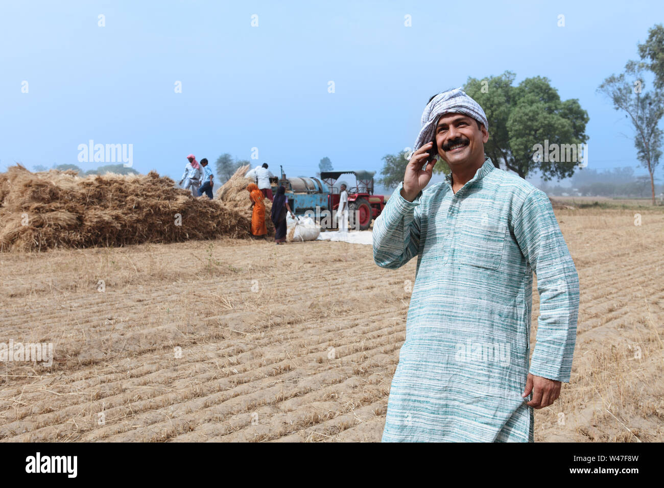 Farmer smiling in a field with farm workers working in the background ...