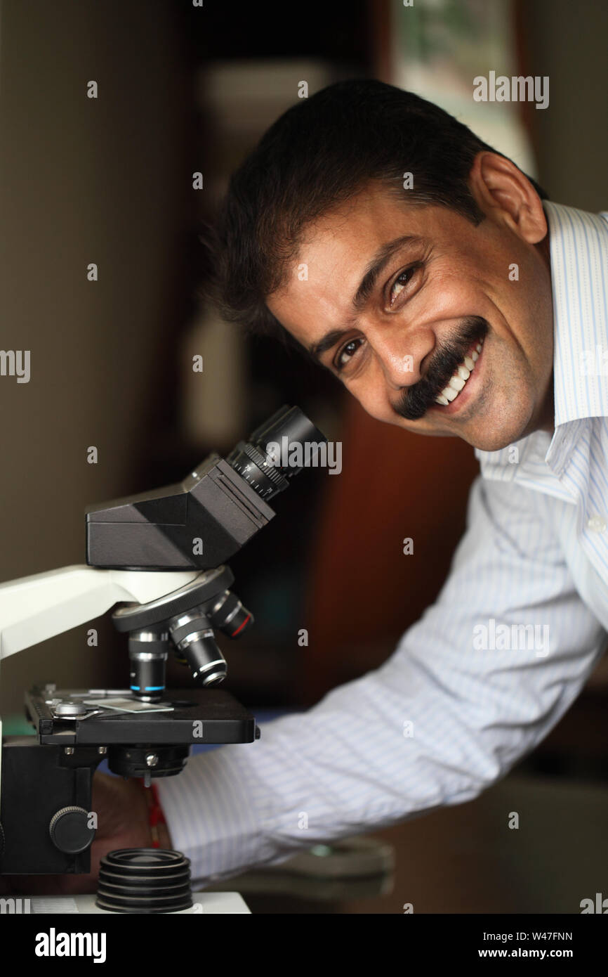 Doctor examining through microscope and smiling Stock Photo - Alamy
