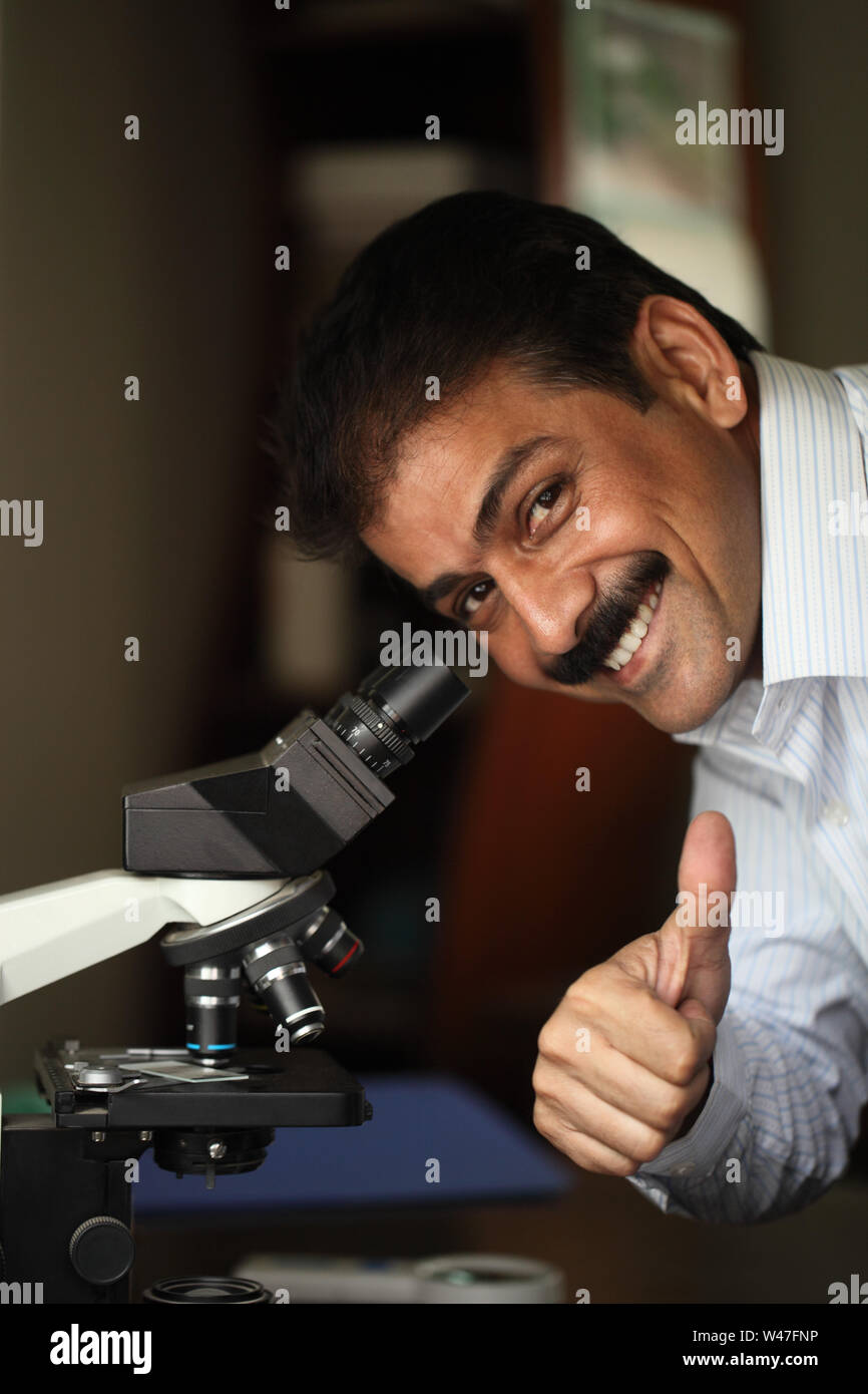 Indian doctor examining through microscope and smiling Stock Photo - Alamy