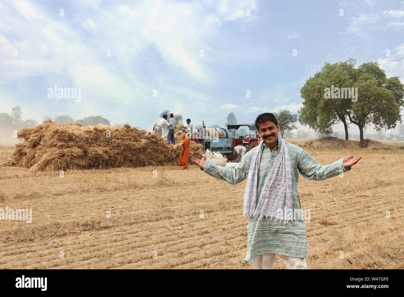 Farmer smiling in a field with farm workers working in the background ...