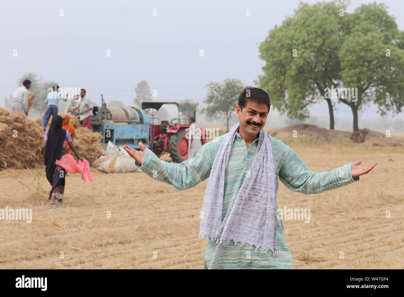 Farmer smiling in a field with farm workers working in the background ...