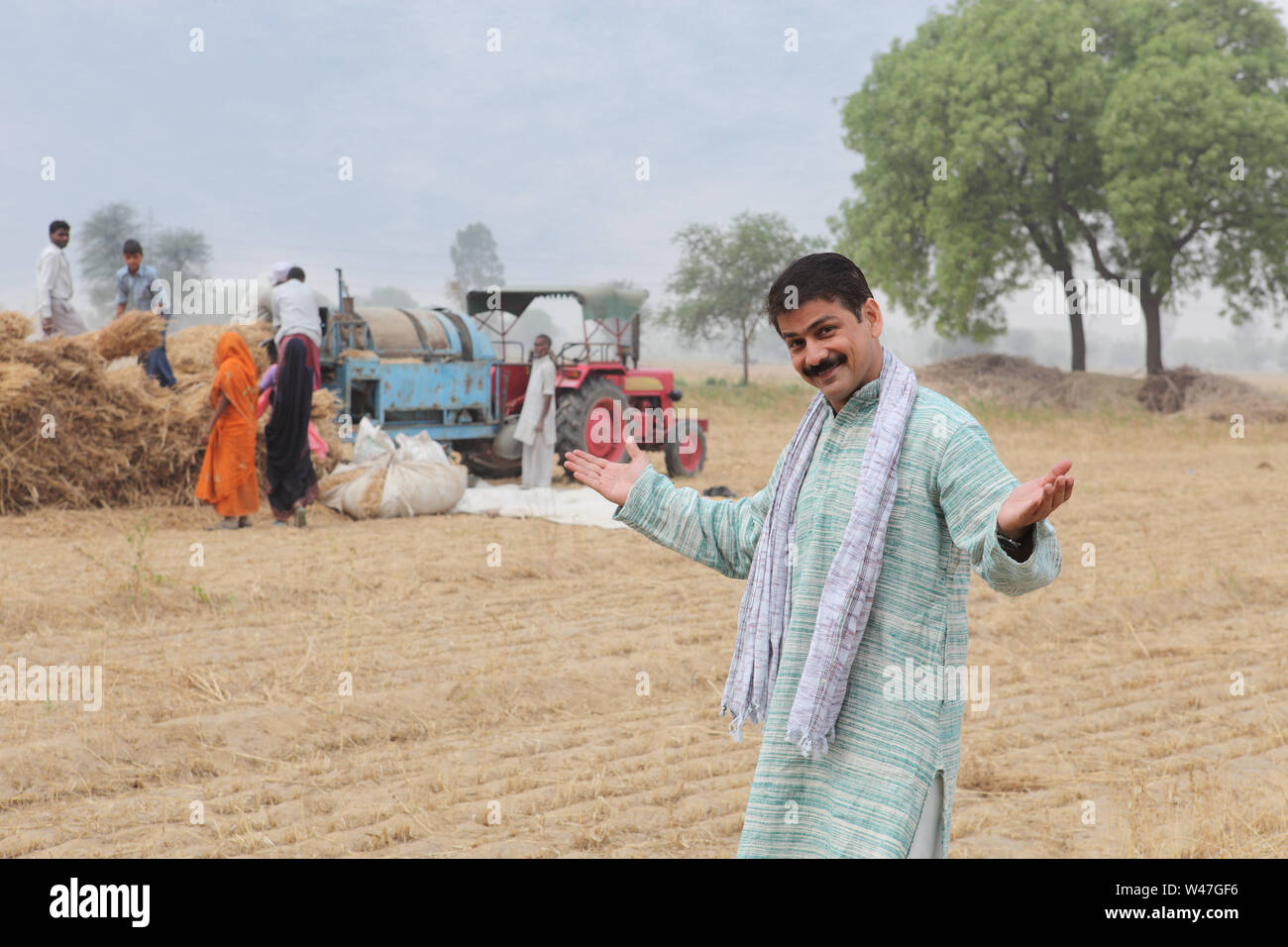 Farmer smiling in a field with farm workers working in the background ...