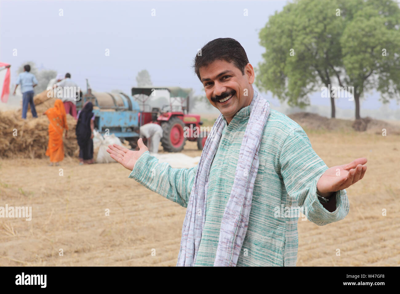 Farmer smiling in a field with farm workers working in the background ...