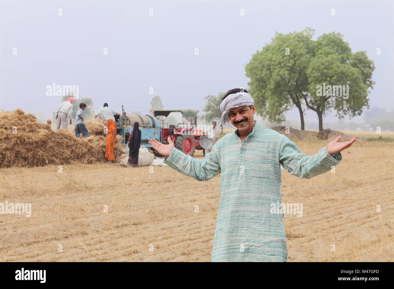 Farmer smiling in a field with farm workers working in the background ...