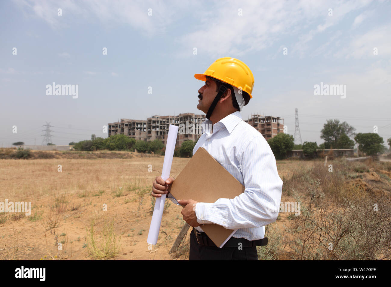 Architect holding a blueprint with construction site in the background ...