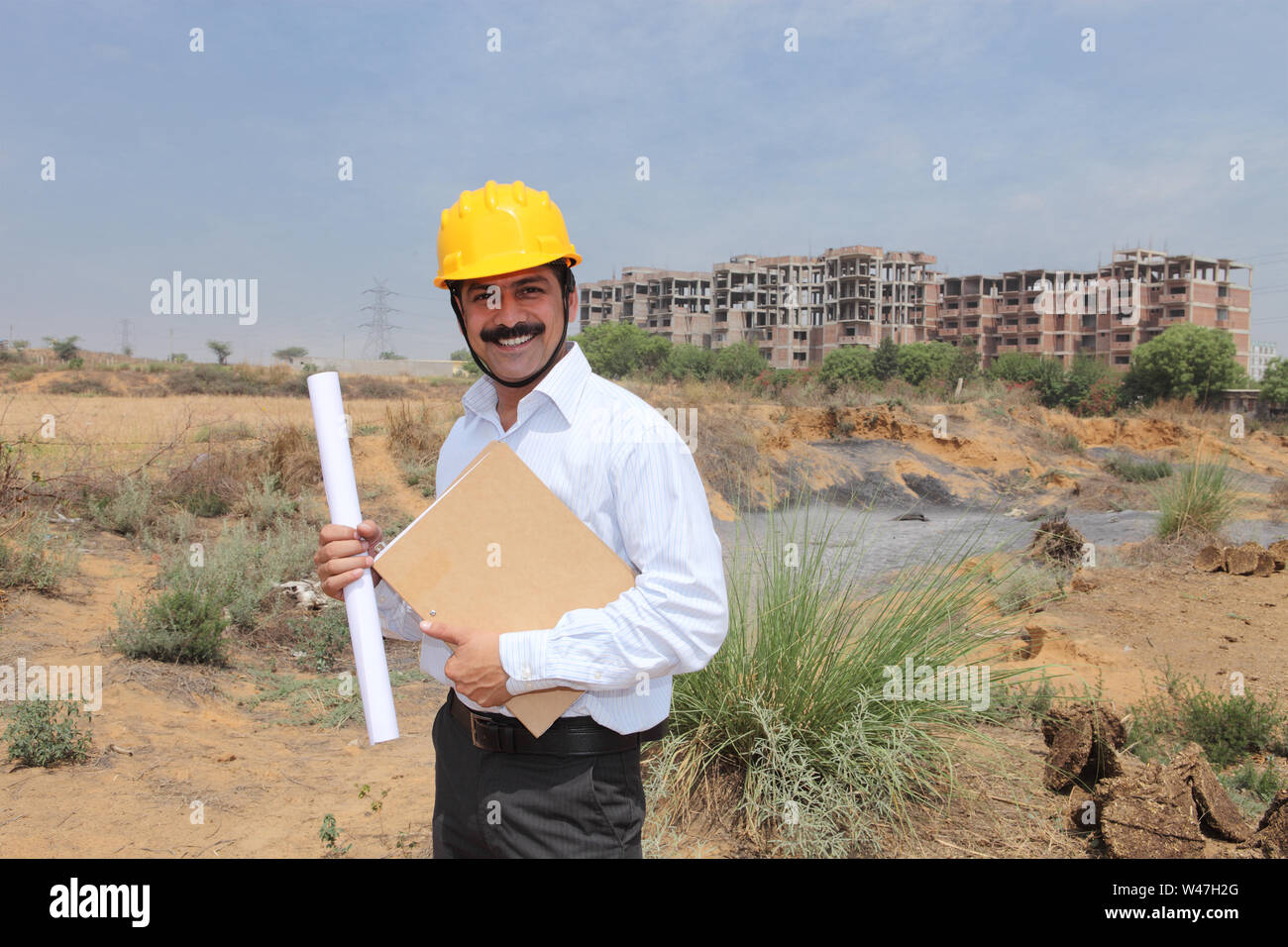 Architect holding a blueprint with construction site in the background ...