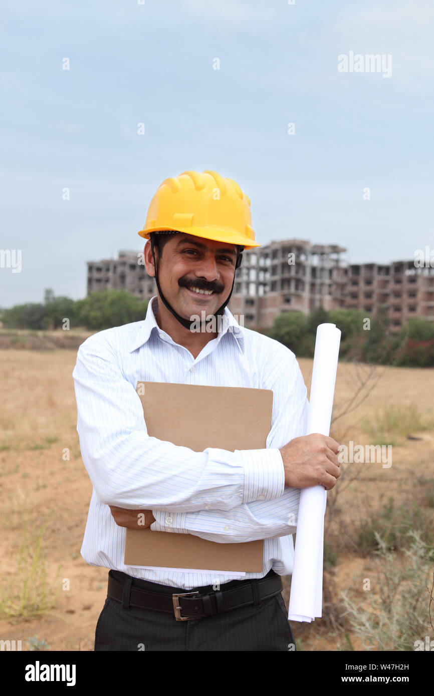 Architect holding a blueprint with construction site in the background ...