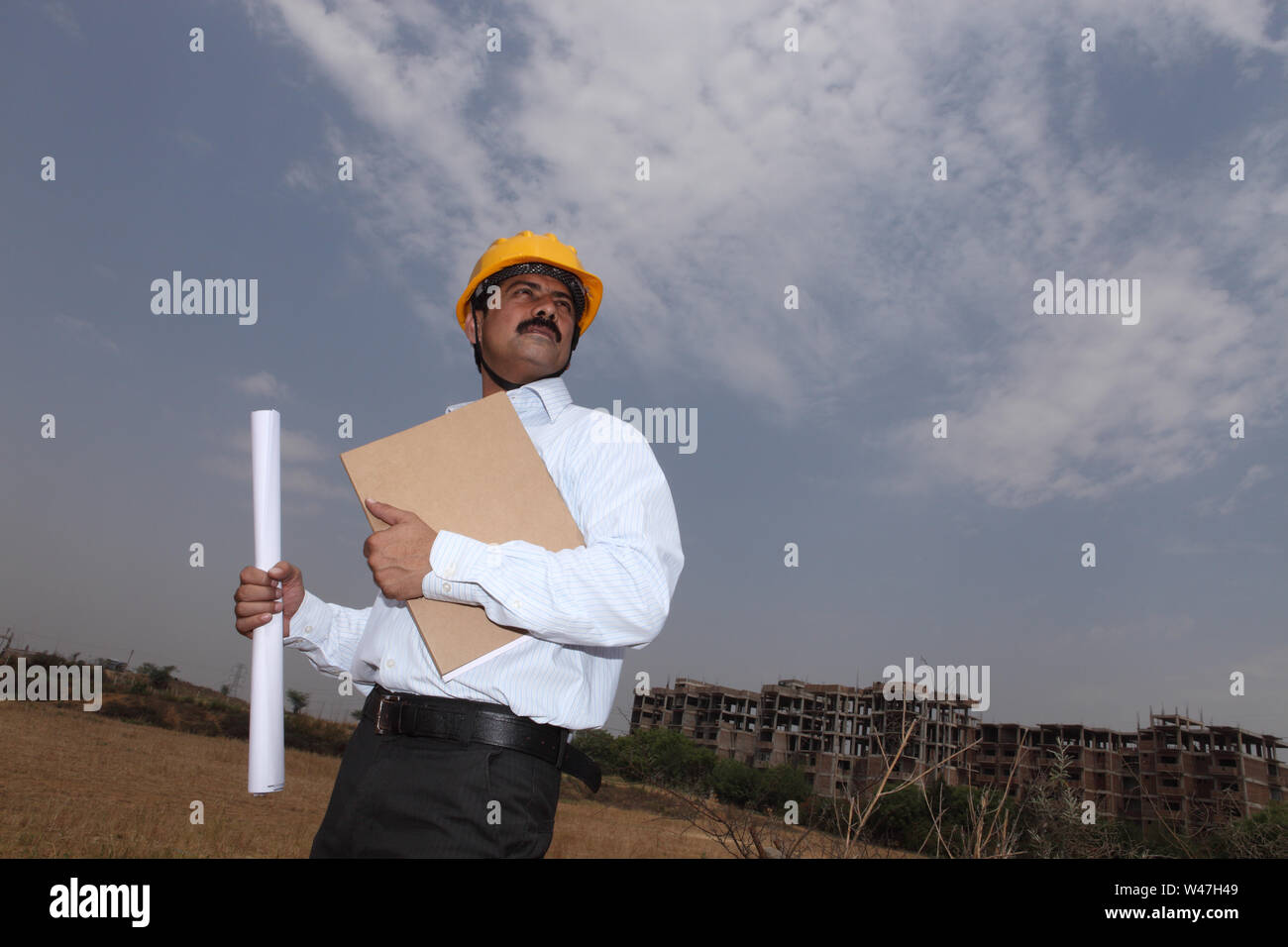Architect holding a blueprint with construction site in the background ...