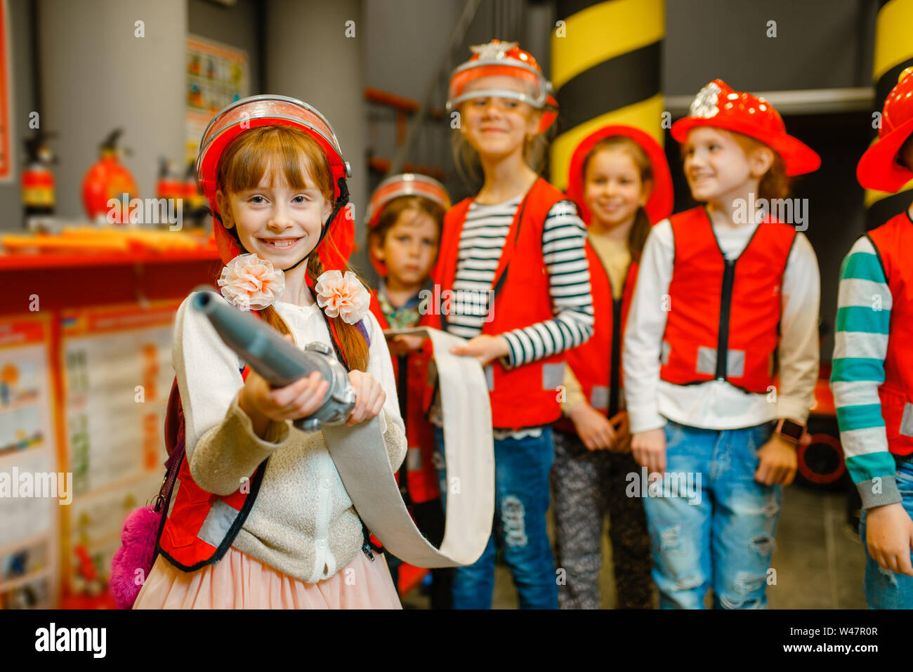 Child in helmet and uniform with hose in hands playing fireman ...