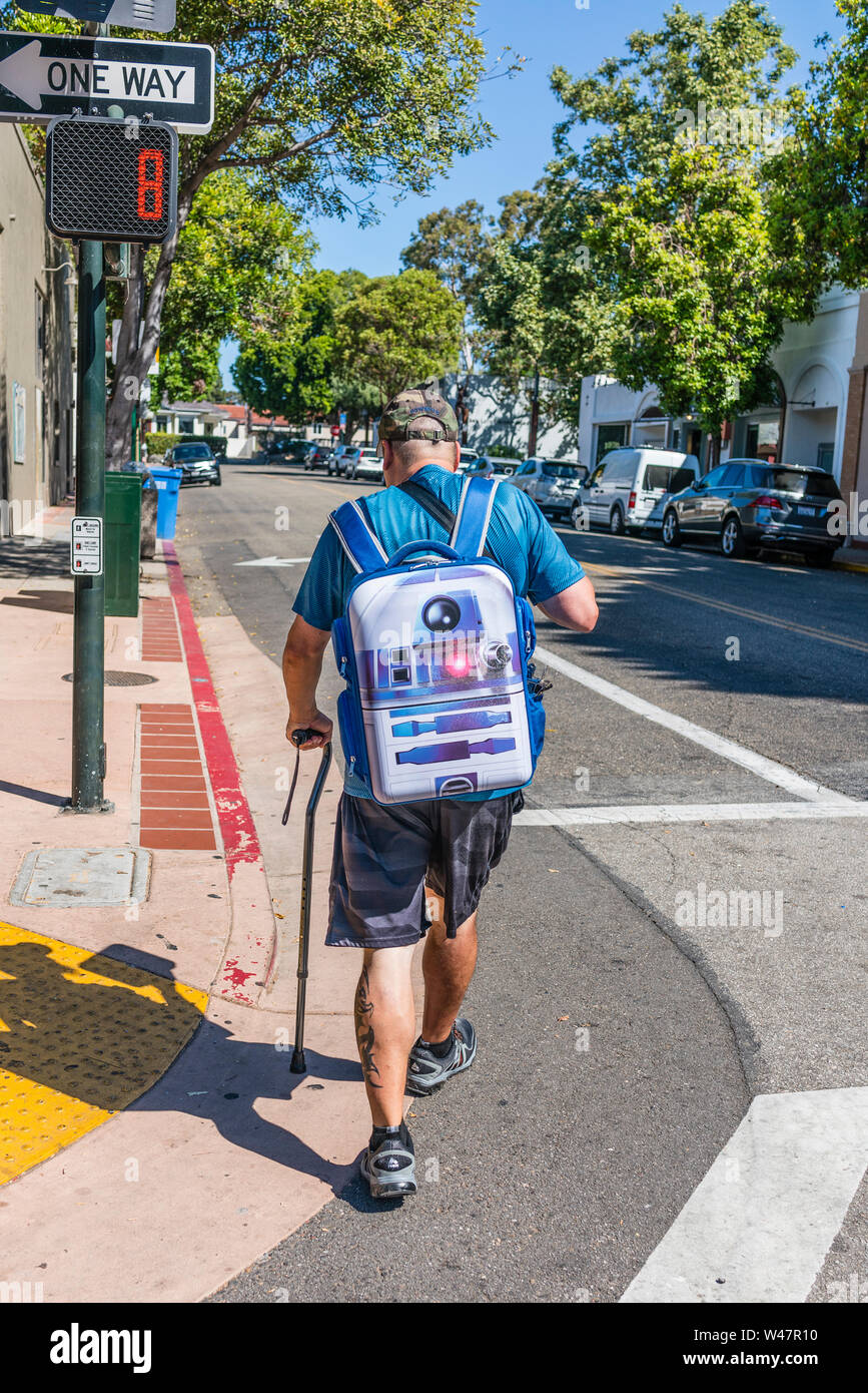 An older male, walking in a crosswalk and using a cane, wears a hard ...