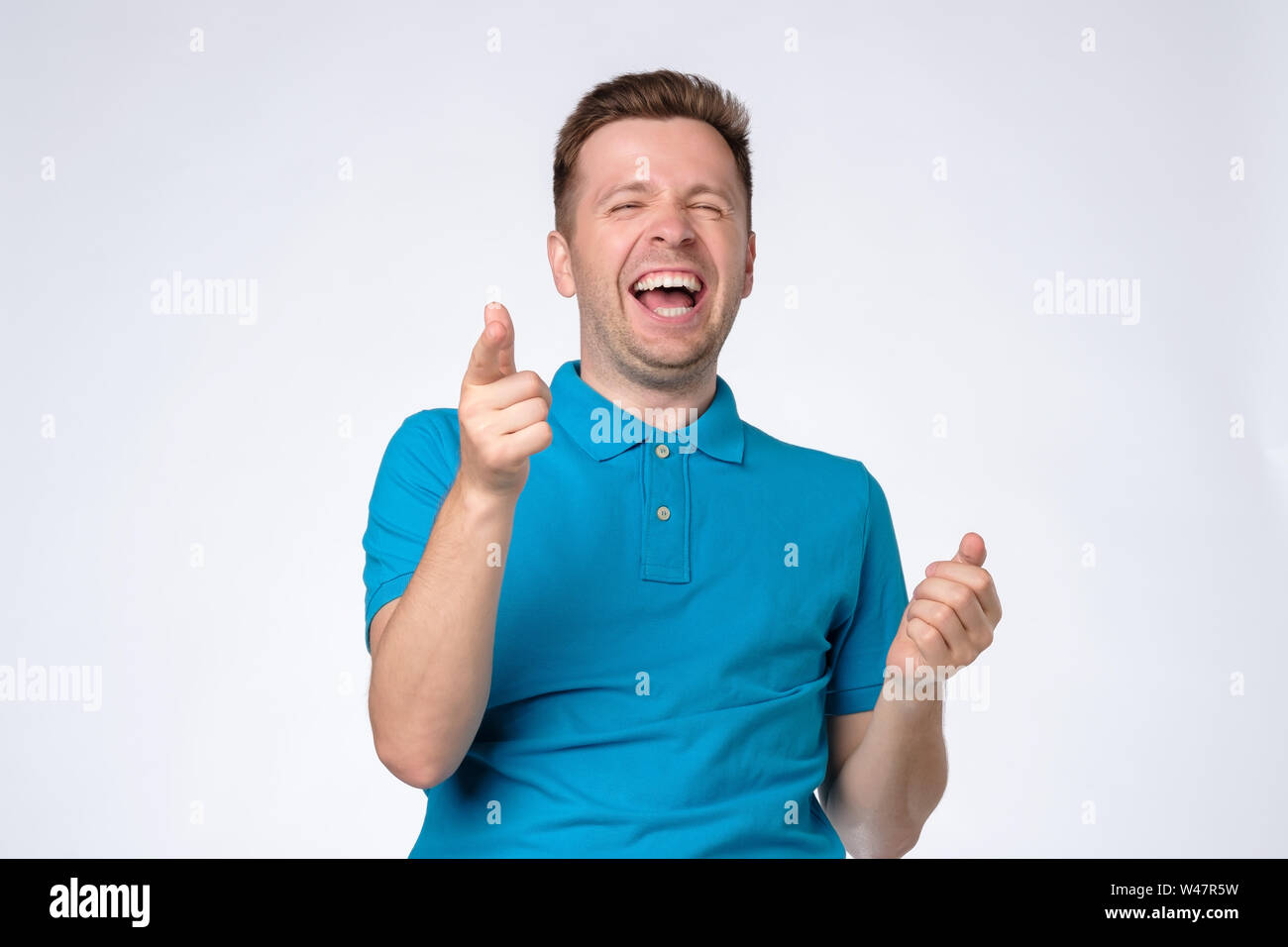 Handsome young man laughing at joke with folded hands. Studio shot ...