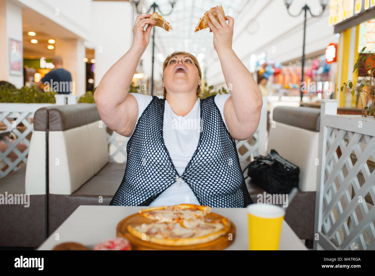 Fatty woman eating pizza in mall restaurant, unhealthy food. Overweight ...