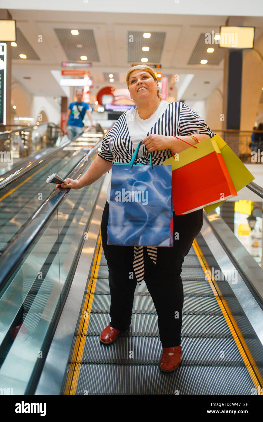 Fat woman with shopping bags on the escalator in mall. Overweight ...