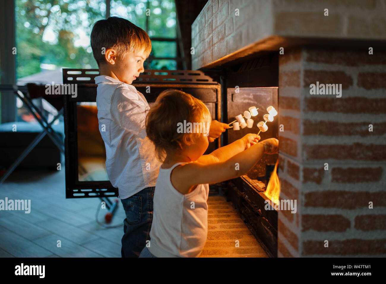 Little kids frying sausages on sticks at fireplace in their house ...