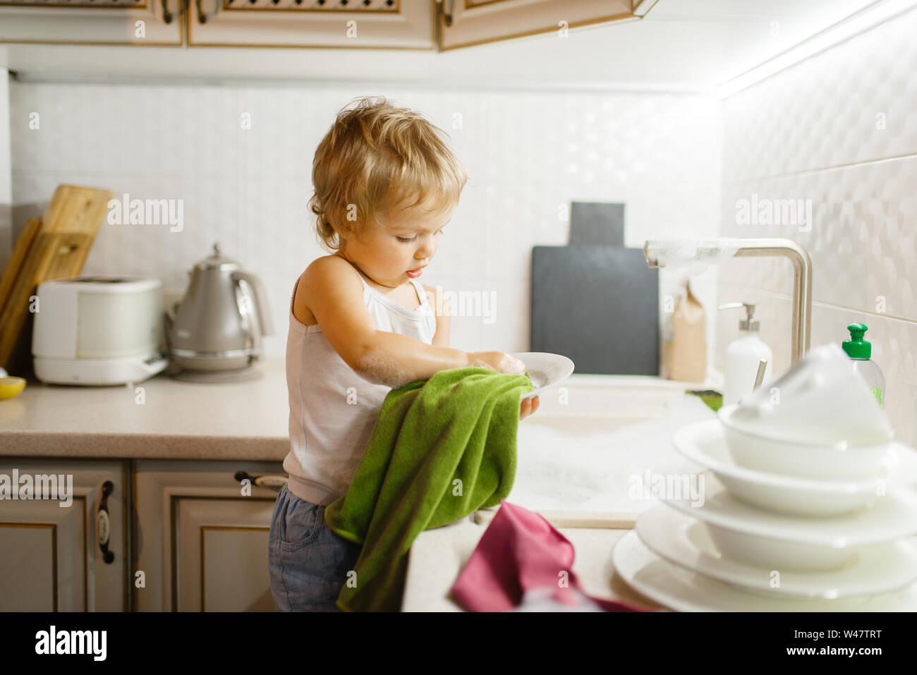 A little girl wipes the dishes on the kitchen. Baby doing housework at ...
