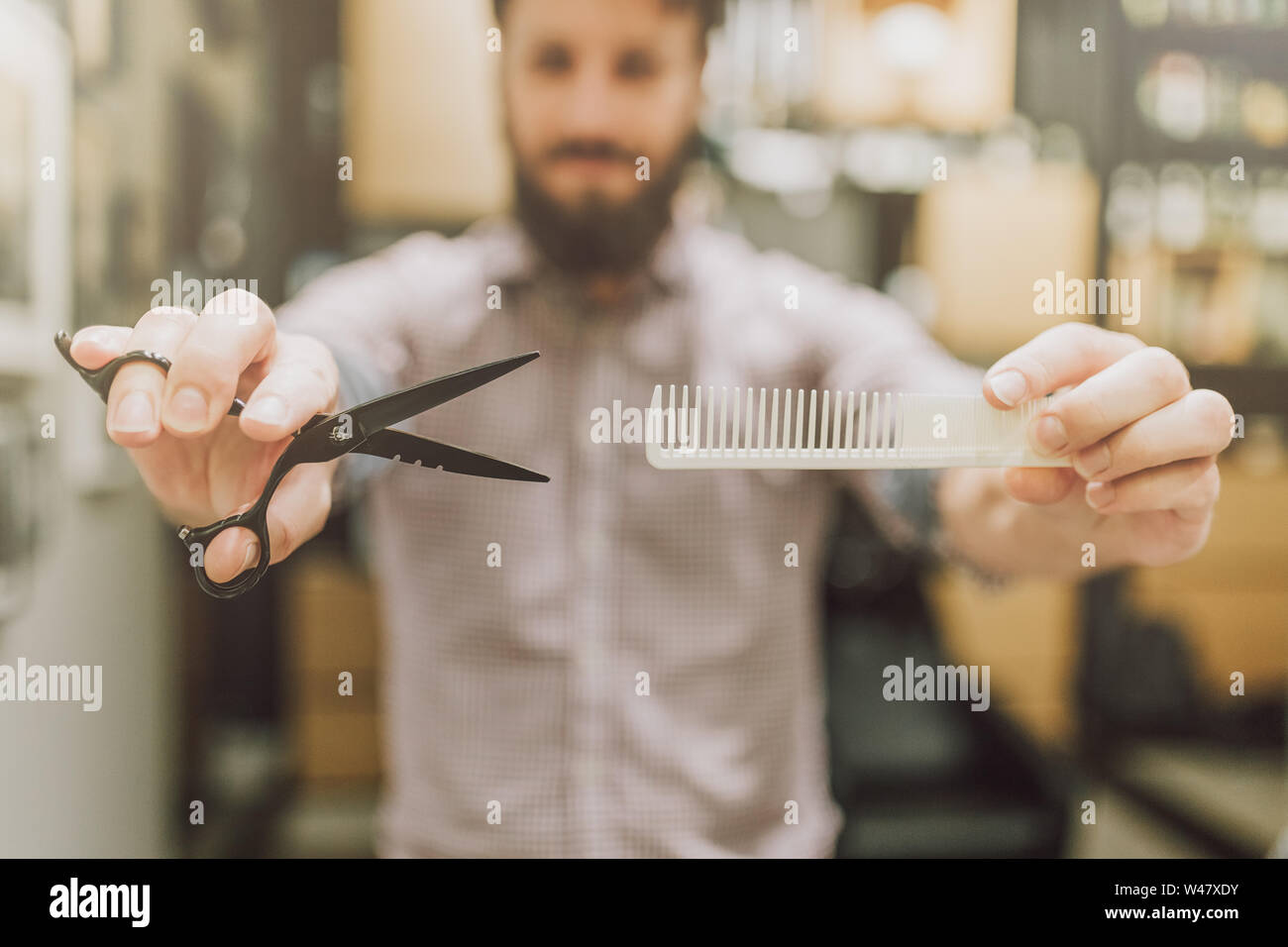 Modern barber holding comb and scissors at barbershop Stock Photo - Alamy