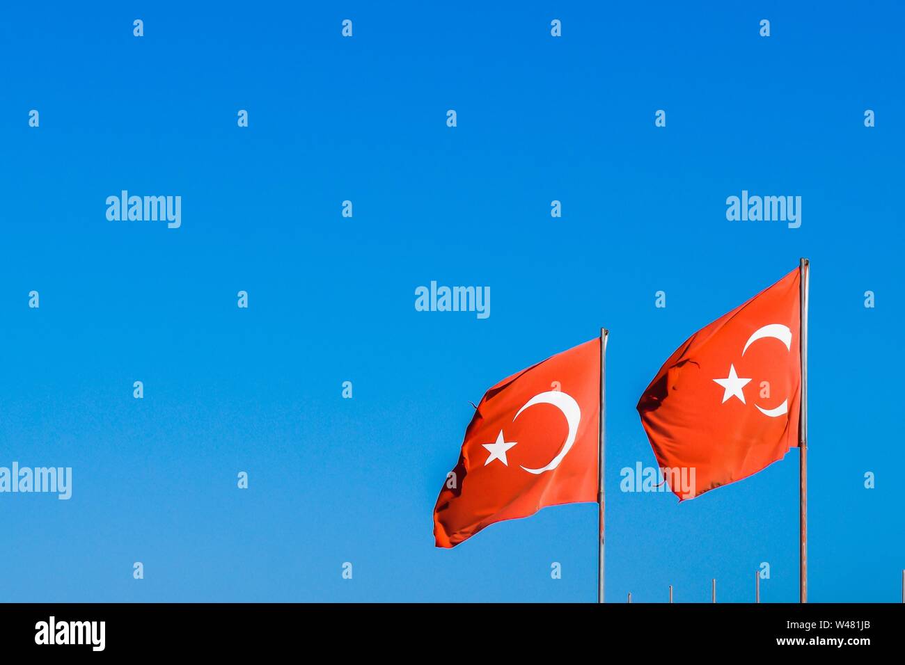 Two Turkish flags waving in the wind, with a bright blue sky as the ...