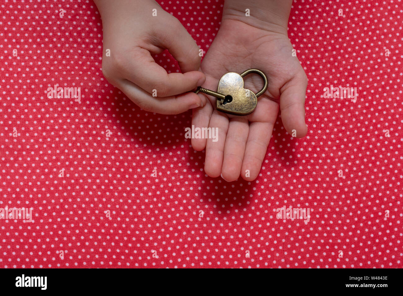 Hand holding a heart shaped lock and key on a red background Stock ...