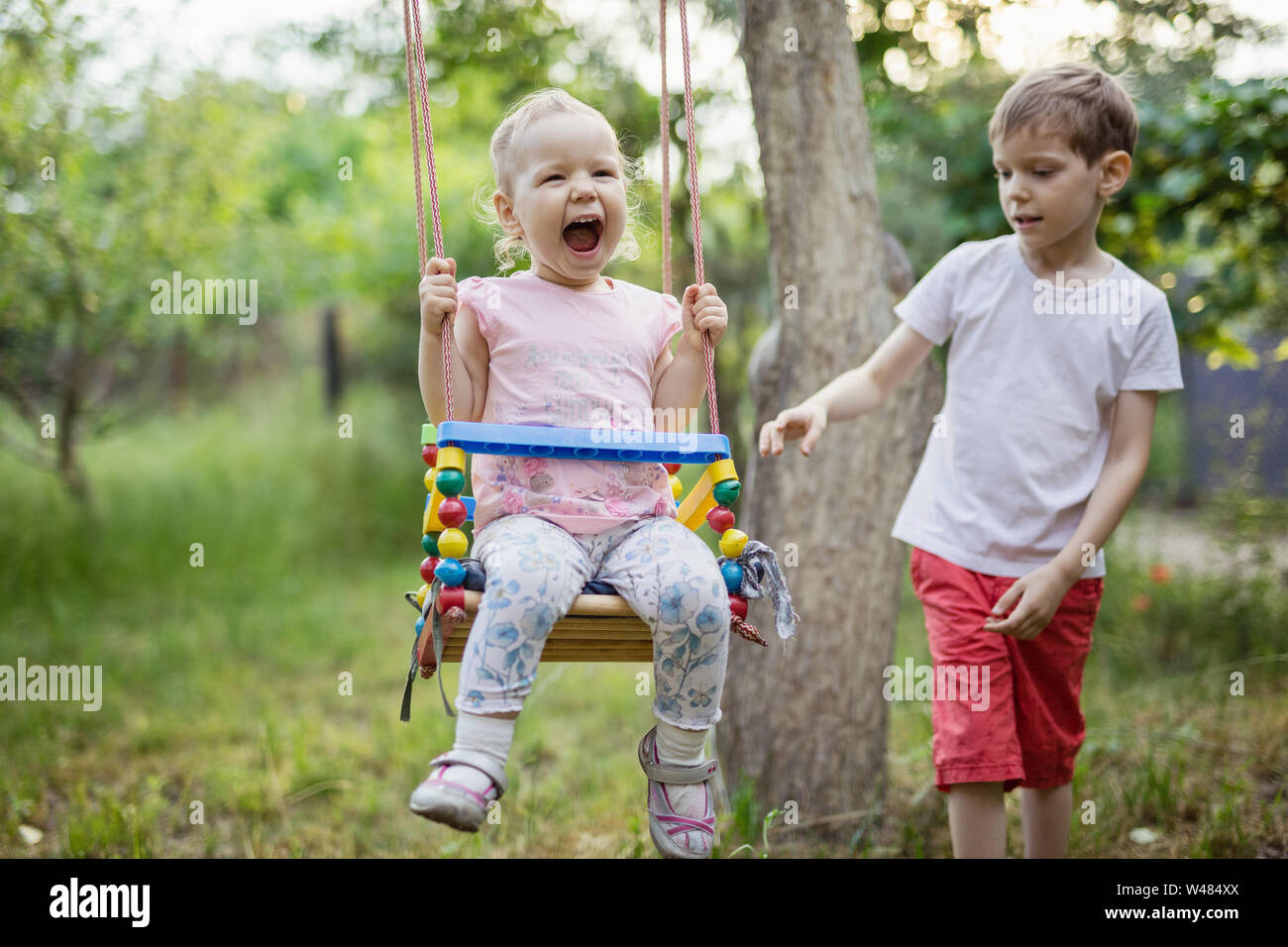Young boy pushing toddler sister on swing. Siblings having fun outdoors ...