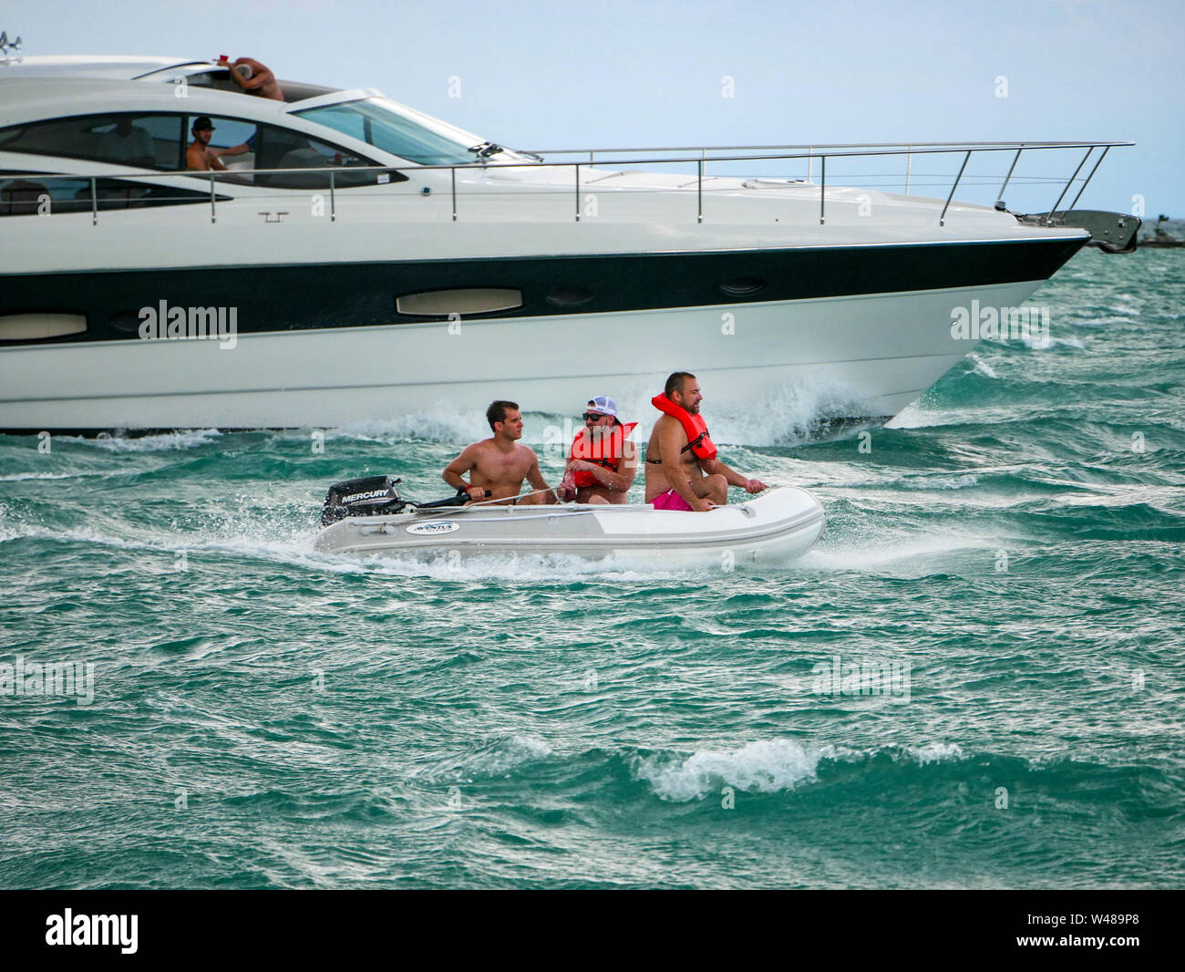 Men in a motorized inflatable dinghy passing large cabin cruiser in ...