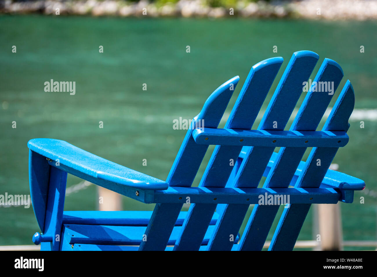 A blue wooden lawn chair on the waterfront riverwalk on a sunny day ...