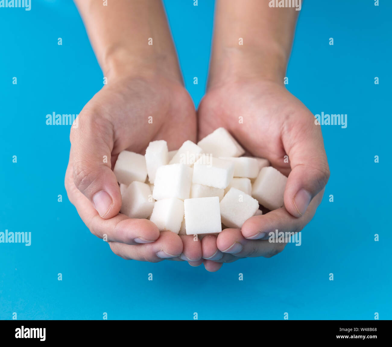 Human hand holding a sugar cube in hand with a blue background Stock ...