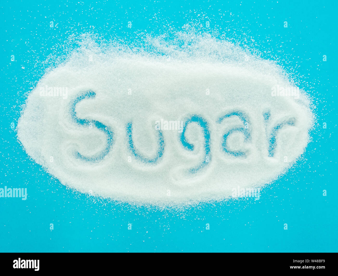 The word sugar written into a pile of granulated sugar on blue ...
