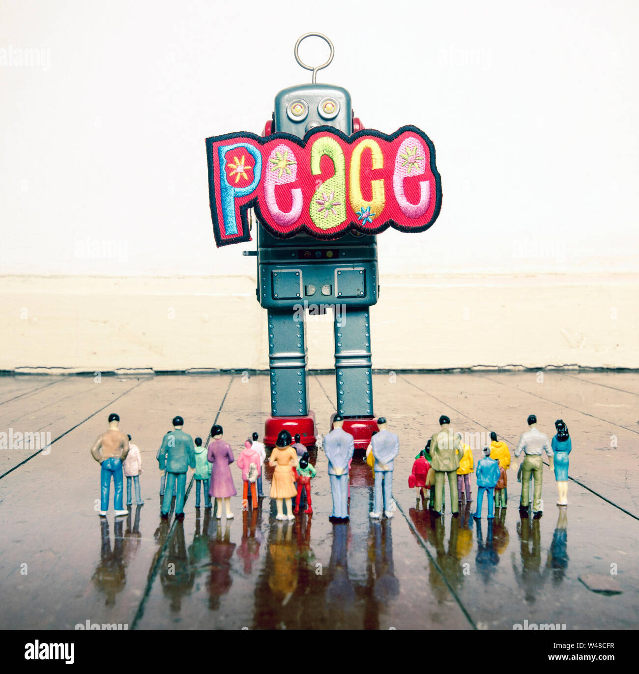 a big robot holding a peace sign to a crowd of plastc people on a old ...