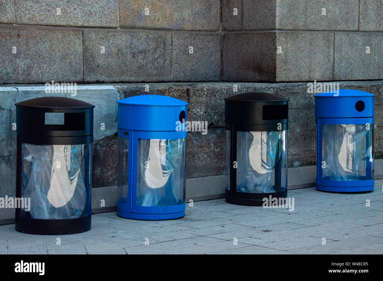 Two black garbage bins and two blue recycle bins. Public waste trash ...