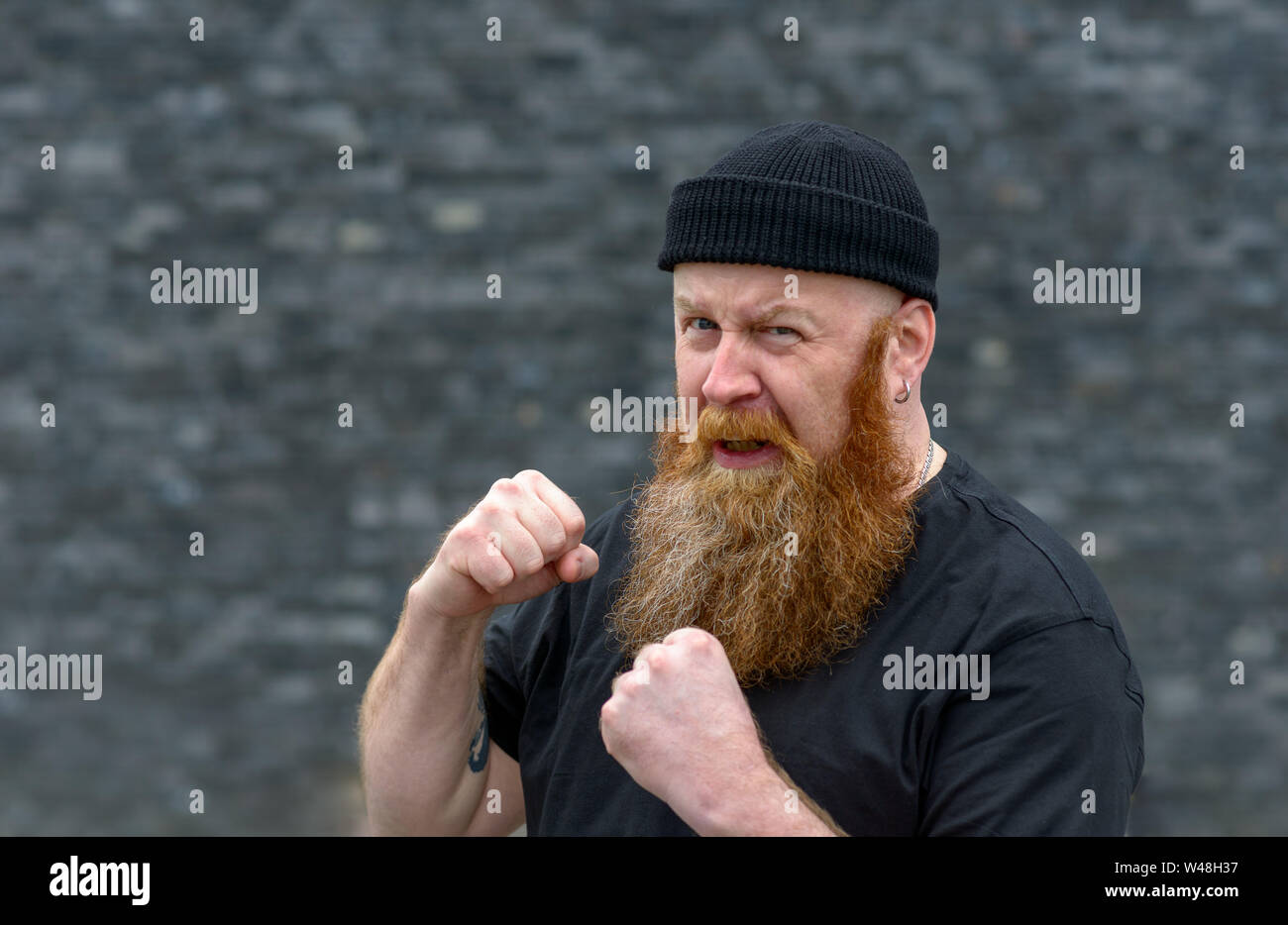 Angry aggressive man with bushy red beard in a knitted beanie hat ...