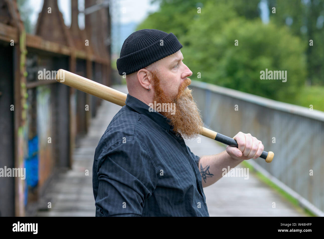 Side view of an bearded man with a baseball bat blocking access along a ...