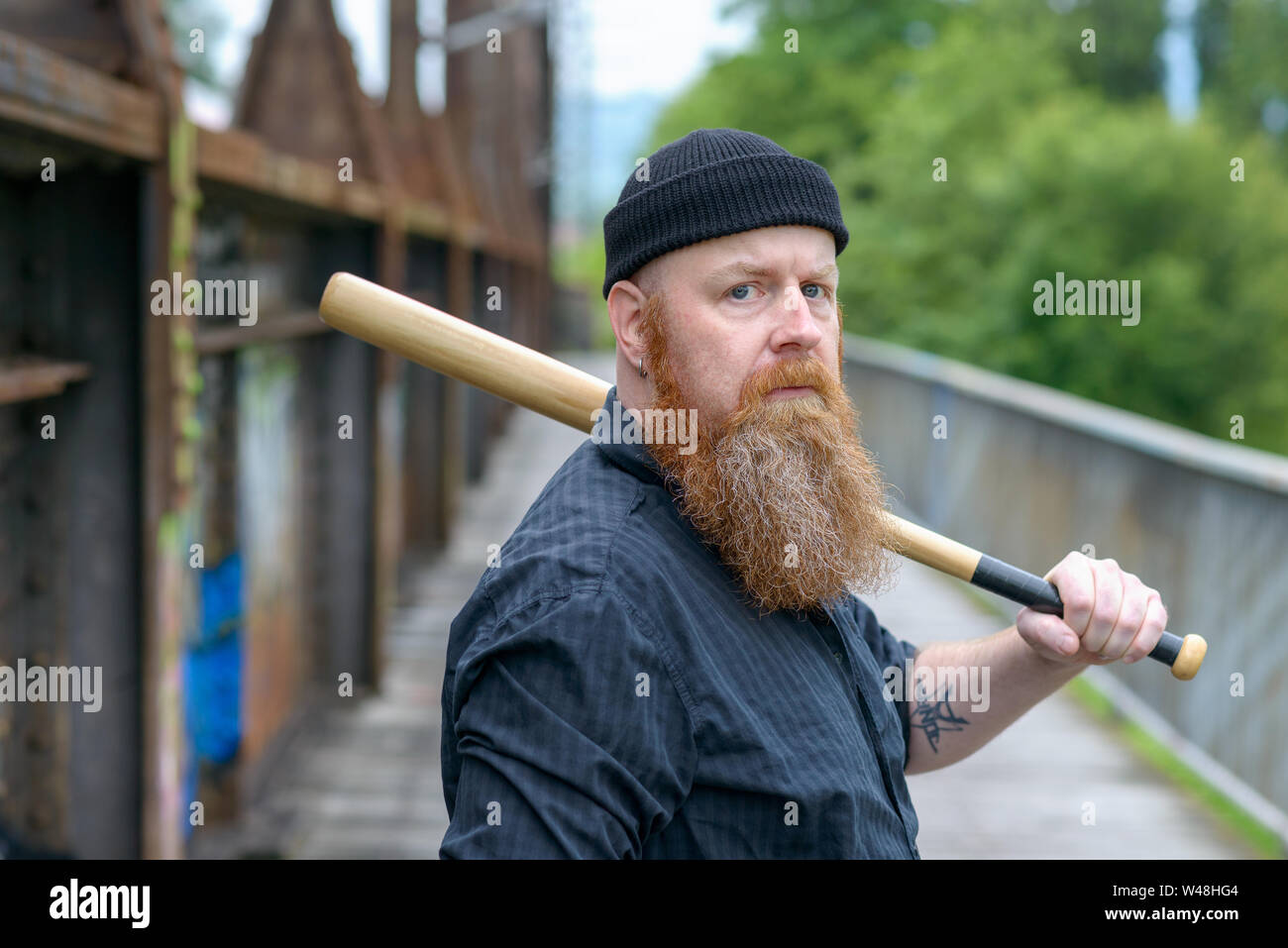 Close up of an bearded man with a baseball bat blocking access along a ...