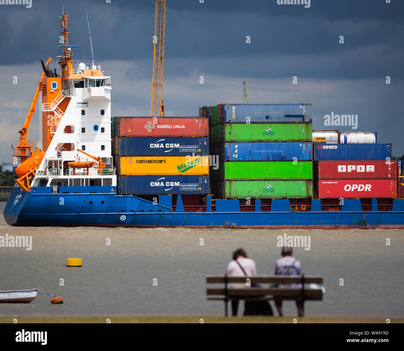Container ship heads out to sea along the River Thames estuary. People ...