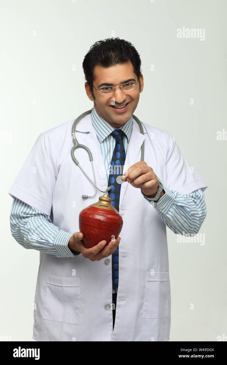 Male doctor inserting a coin into a piggy bank and smiling Stock Photo ...
