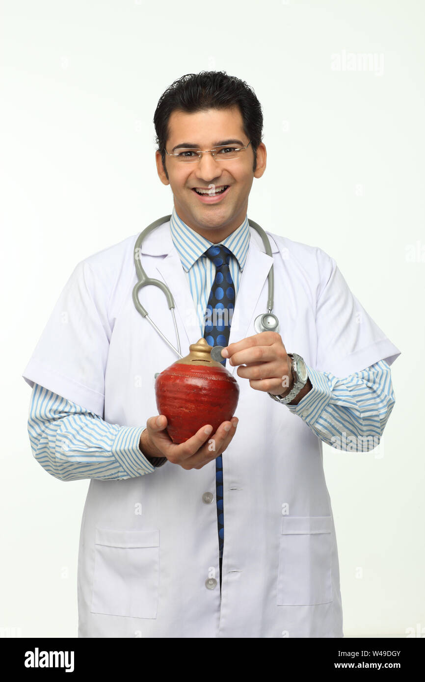 Male doctor inserting a coin into a piggy bank and smiling Stock Photo ...