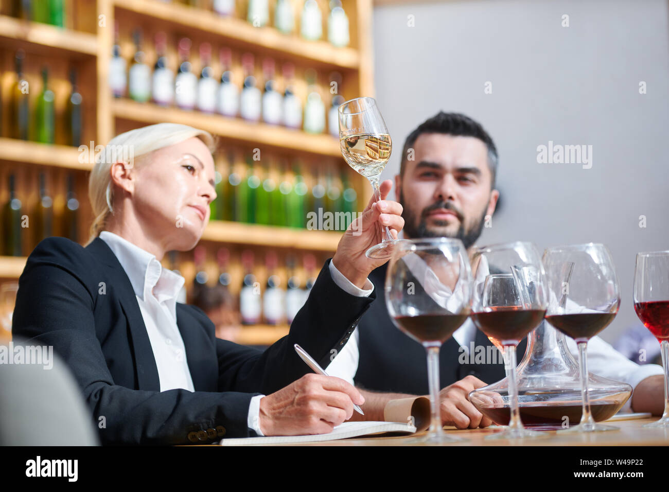 Serious professional sommeliers examining color of white wine in bokal ...