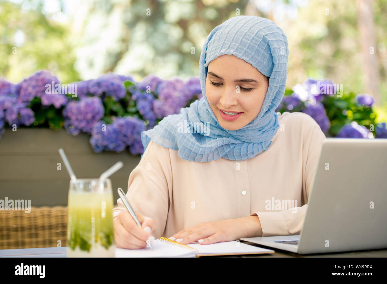 Pretty muslim student in hijab making notes in notebook outdoors Stock ...