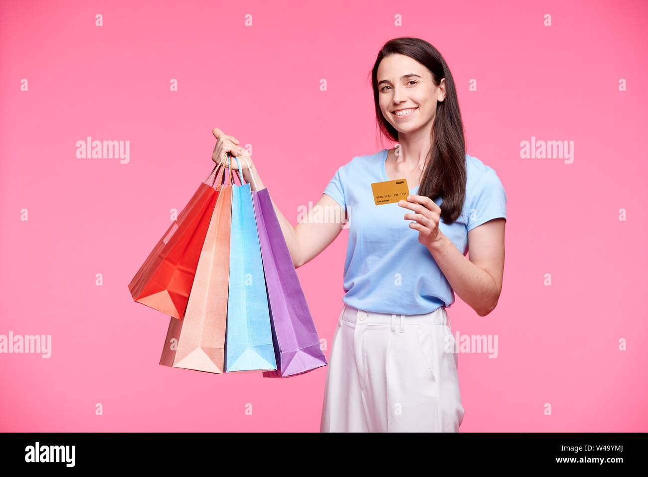 Young cheerful shopper with several paperbags showing plastic card ...