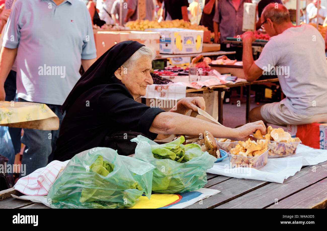Woman dressed in black, selling mushrooms from a table stall at farmer ...