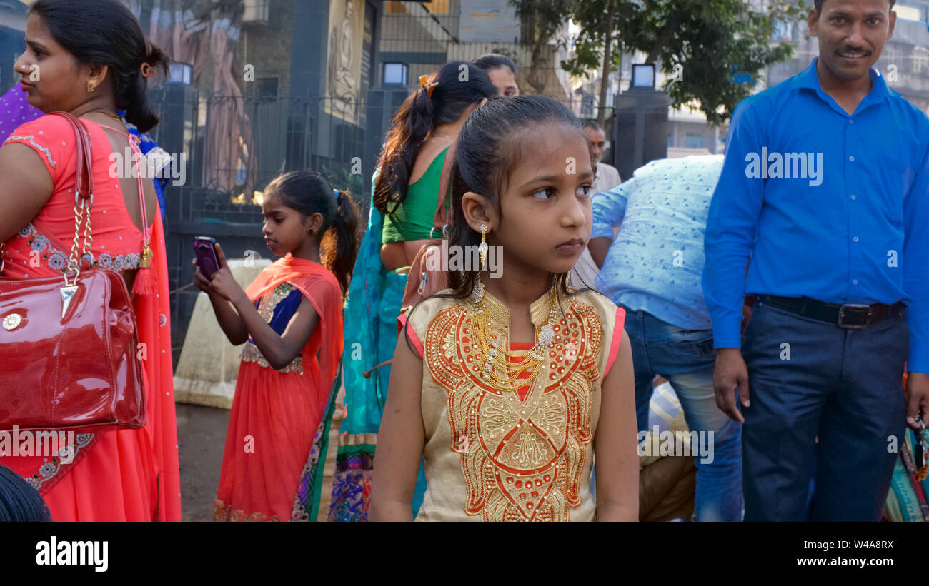 A young Indian girl in neat traditional dress stands apart from her ...