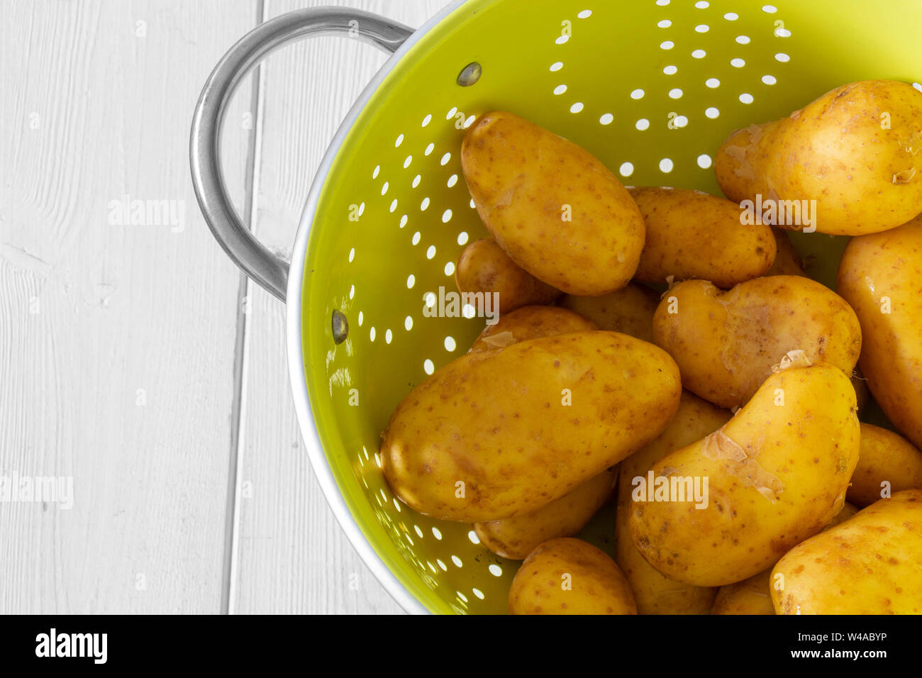 Potatoes, washed, in a bright green metal colander. On a white wood ...