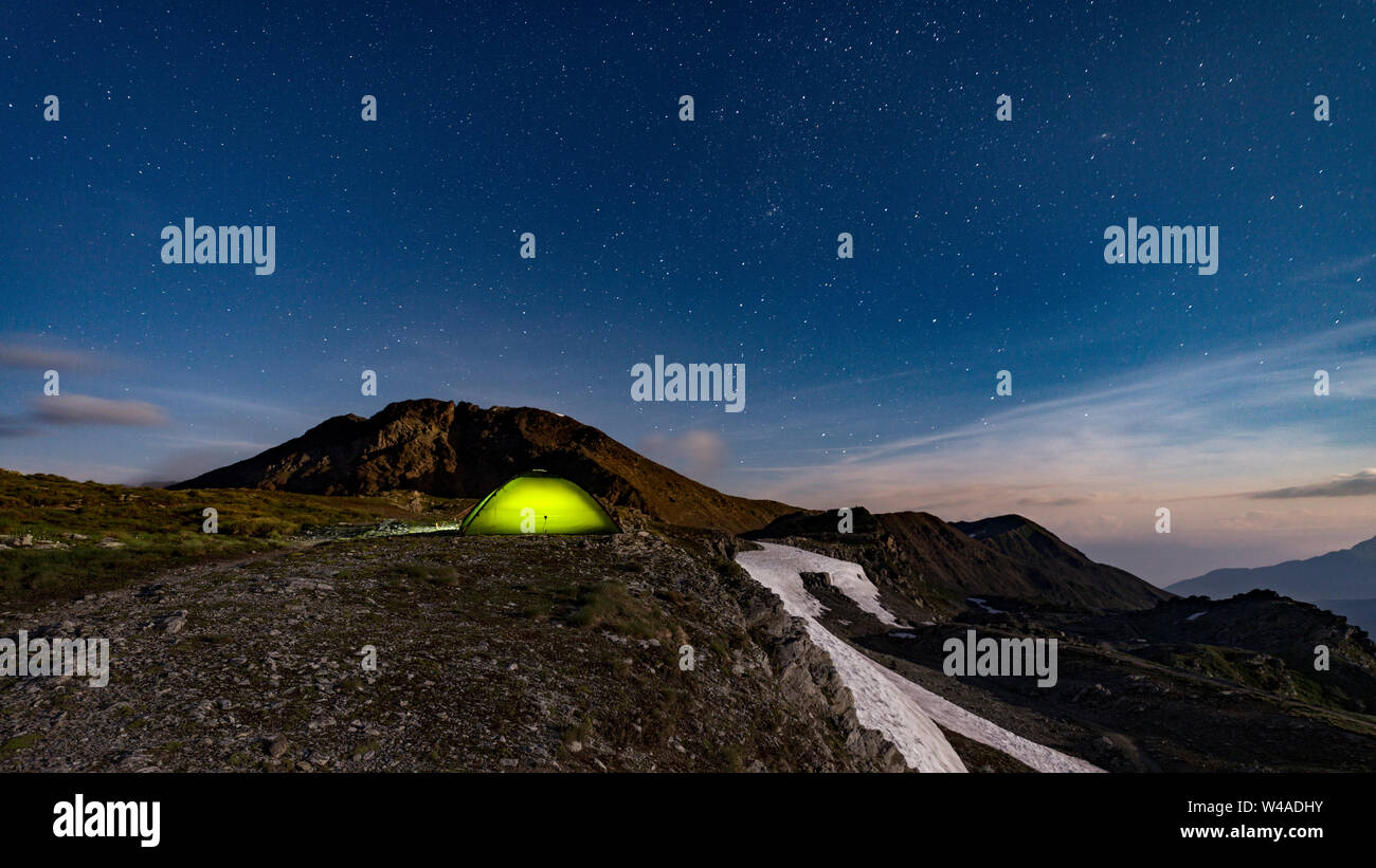 Moonlit scene with illuminated green tent under starry night - fog ...
