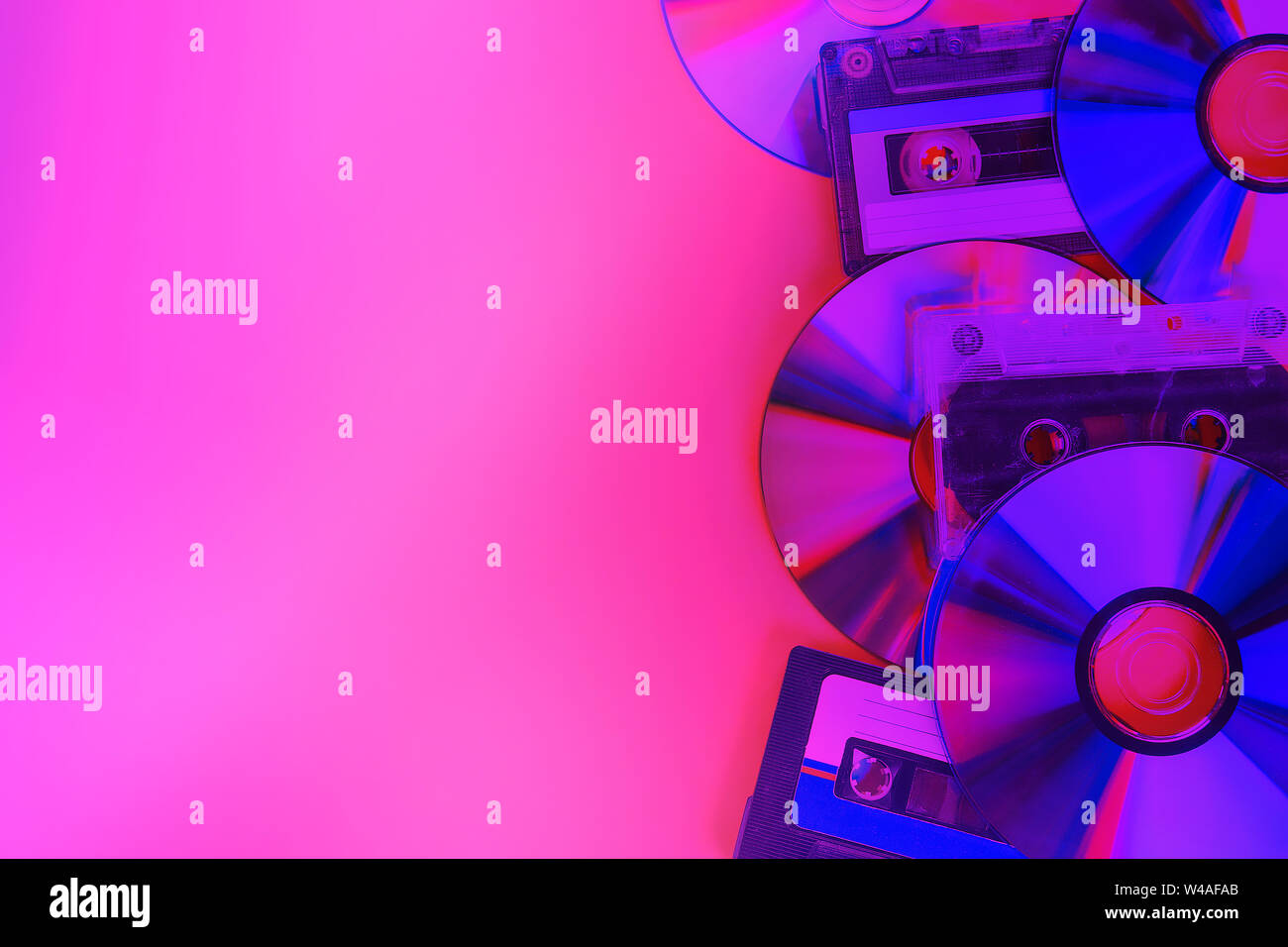 CD disks and audio cassettes on a pink violet purple neon background ...