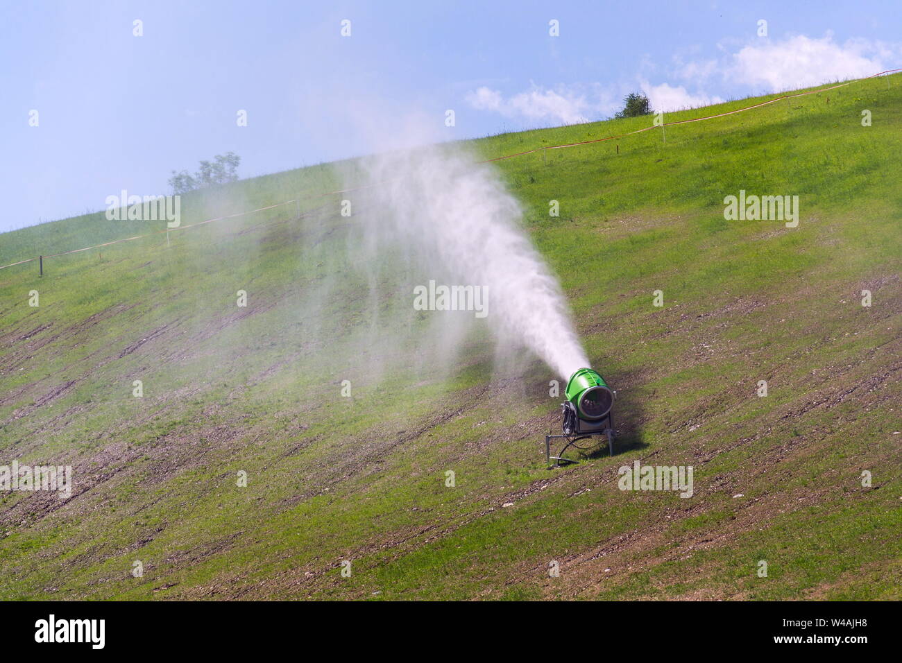 Snow making machines used to water grass on slope, sunny summer day ...