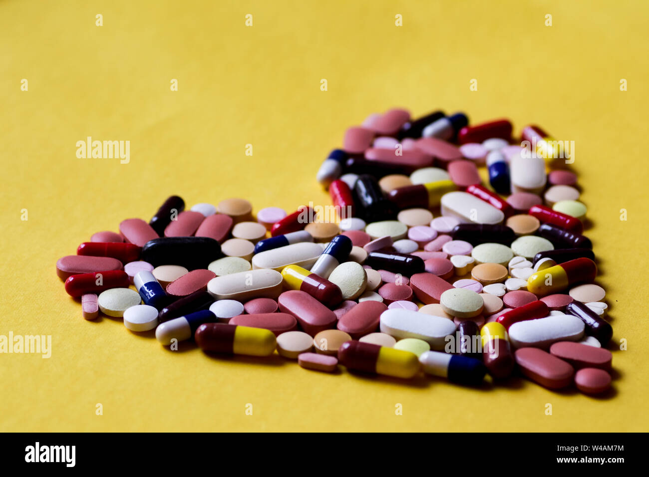 Medicine pills tablets capsules in shape of human heart in yellow ...