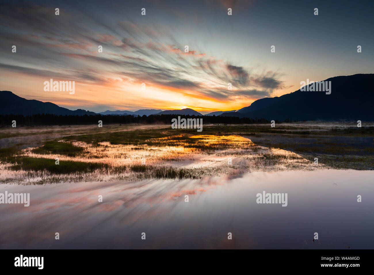 Spectacular sunrise over marshlands with mountain range in background ...