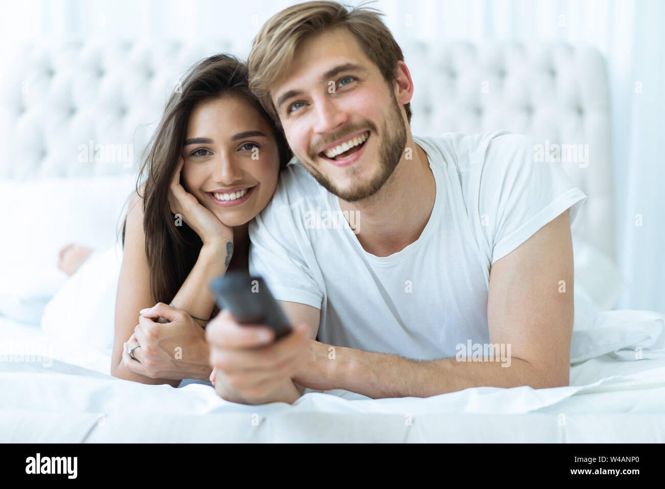 happy couple with remote lying in bed at home and watching tv Stock ...