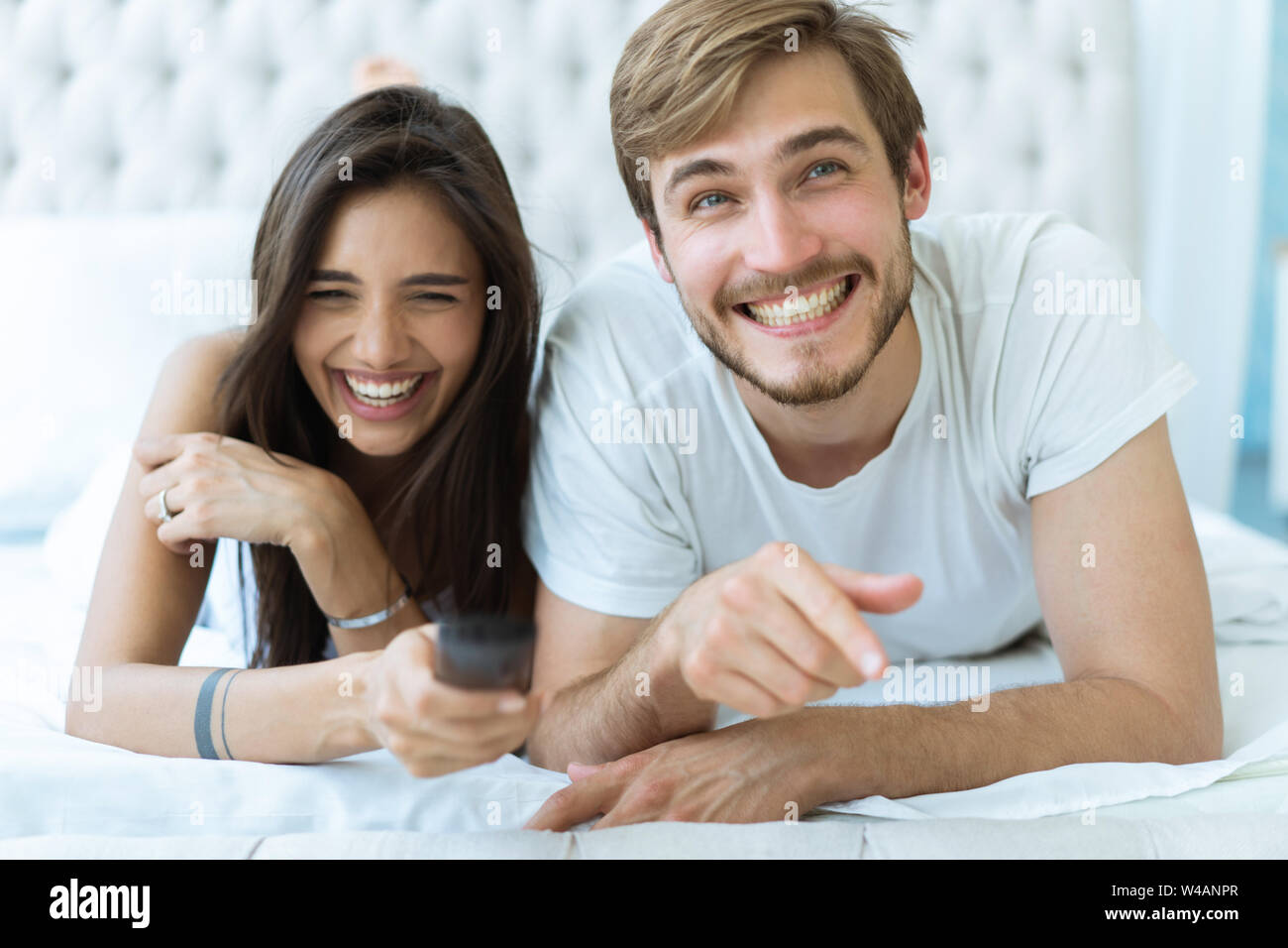 happy couple with remote lying in bed at home and watching tv Stock ...
