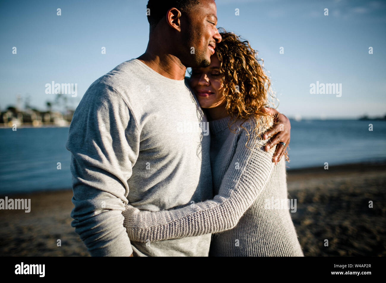 Multi racial couple embrace on beach at sunset Stock Photo - Alamy