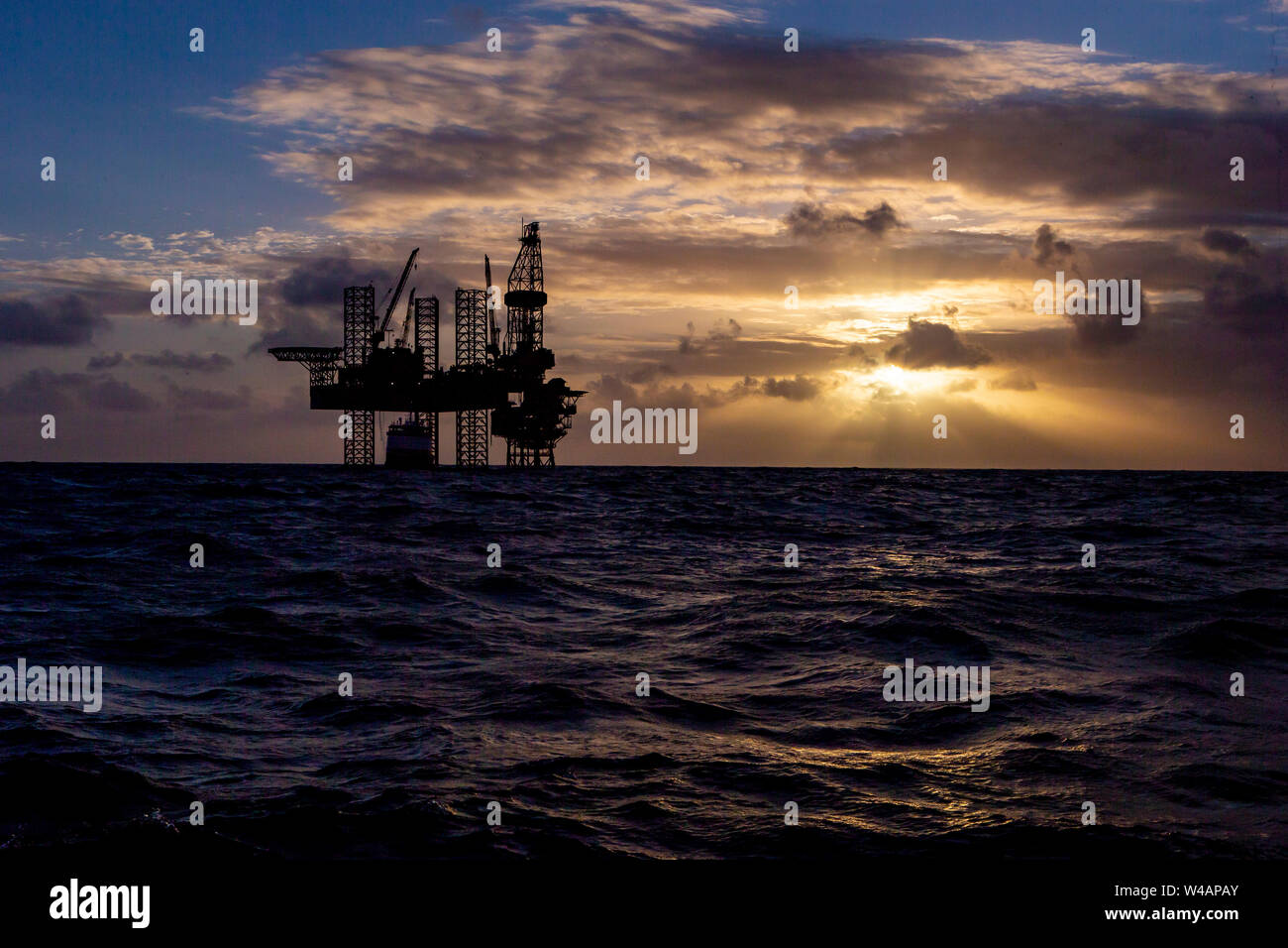 Offshore drilling platform during sunrise with work vessel Stock Photo ...